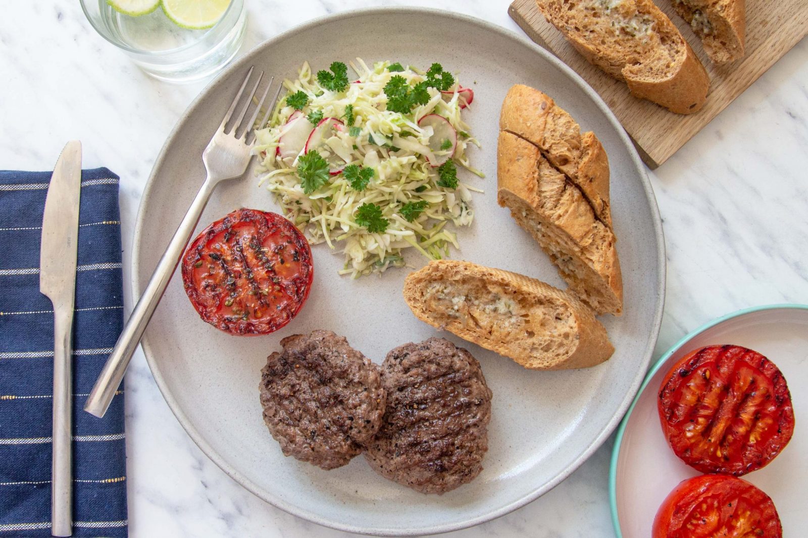 Grilled mince steaks with fried tomatoes and garlic baguette